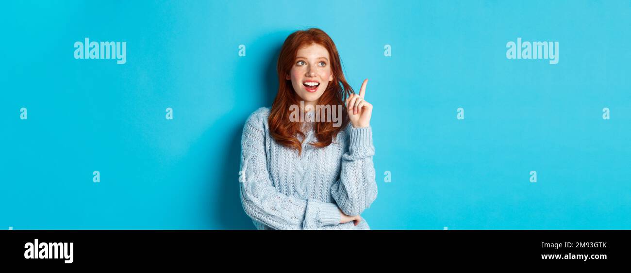 Thoughtful redhead girl having an idea, raising finger and smiling ...