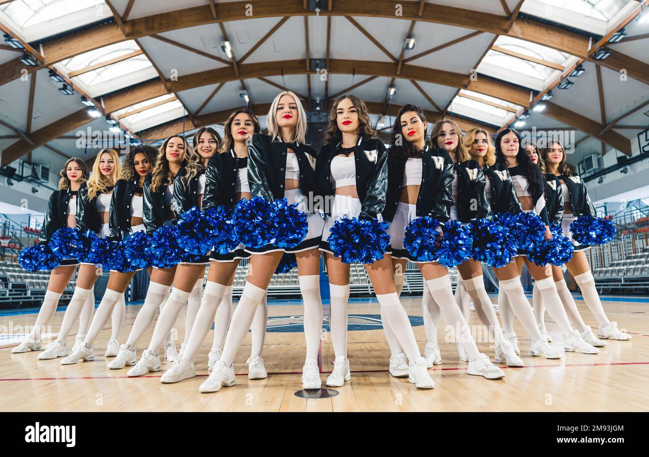 Low-angle shot. Cheerleading V-shaped squad holding blue pom-poms ...