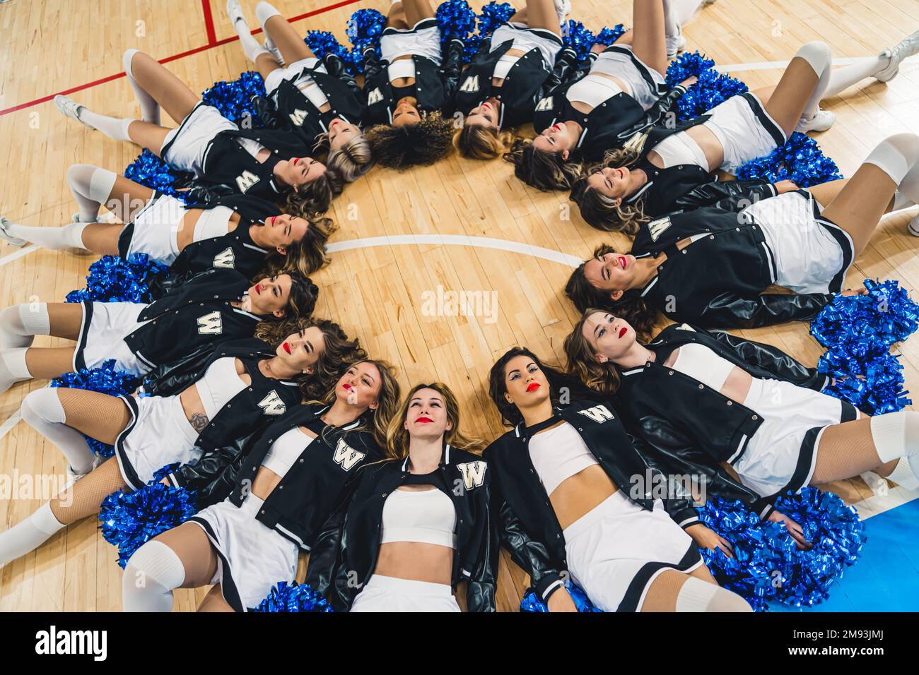Aerial view of a cheerleading squad lying down in the circle and holding pom-poms in their hands ...