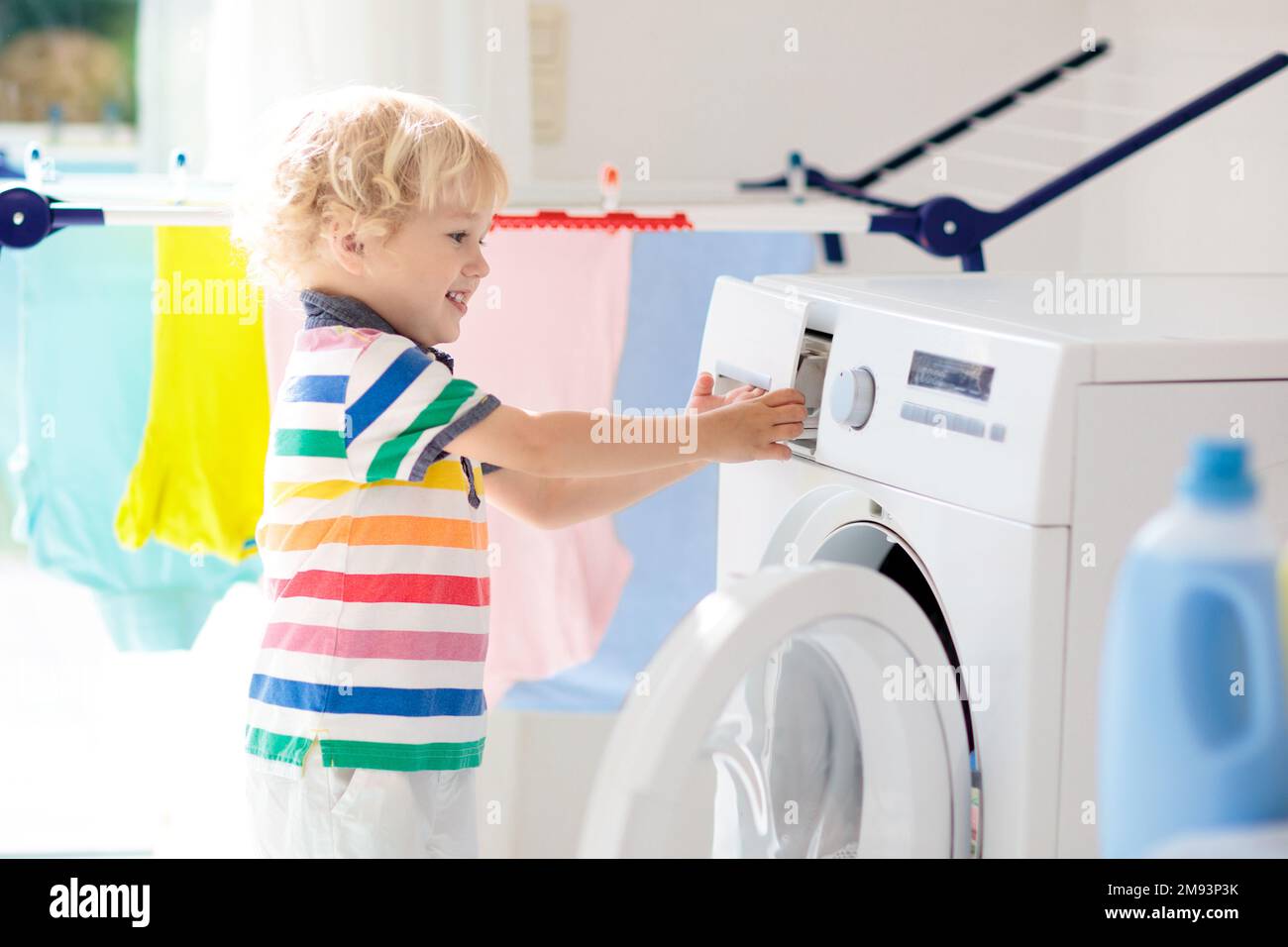 Child in laundry room with washing machine or tumble dryer. Kid helping ...