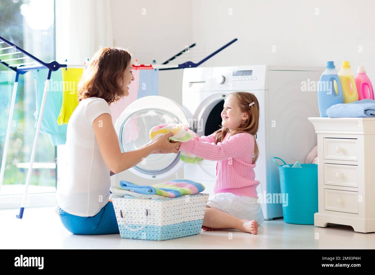 Mother and kids in laundry room with washing machine or tumble dryer ...