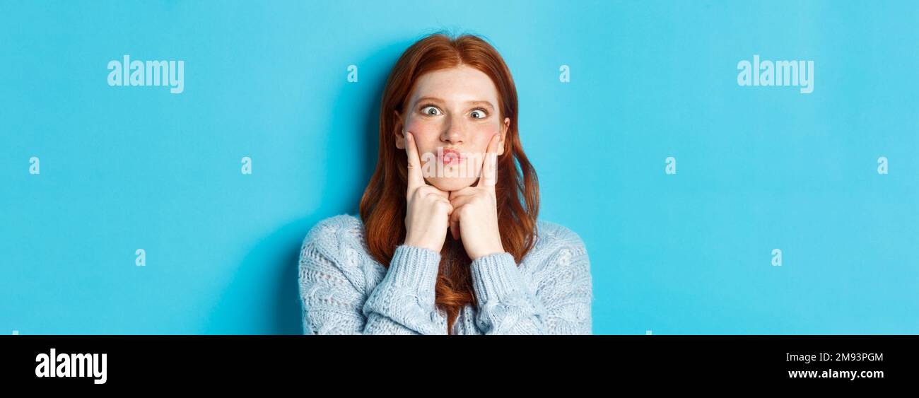 Close-up of funny redhead teen girl making faces, squinting and pocking ...