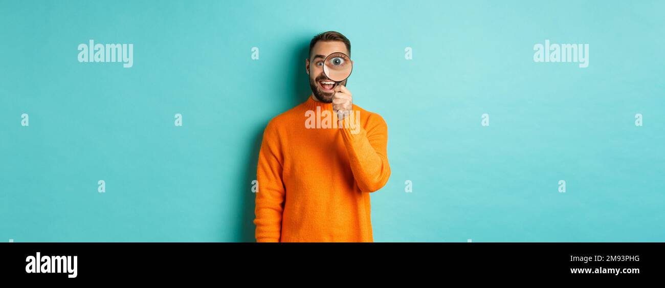 Cheerful man searching for something, looking through magnifying glass ...