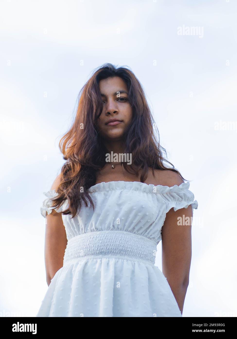 A low angle of a young female in a white summer dress with a skyscape ...