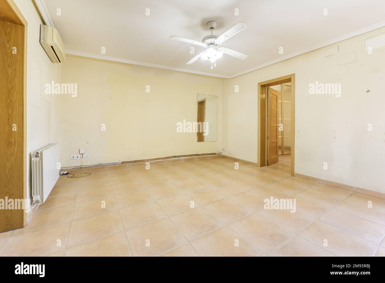 Empty room with brown stoneware floor, white aluminum radiator, mirror ...