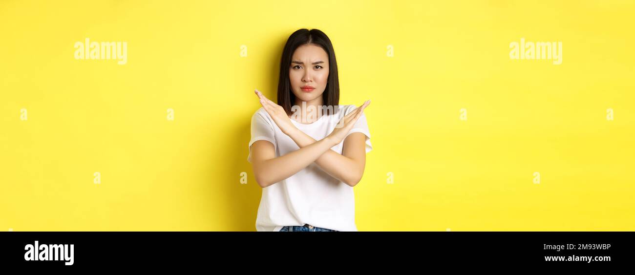Serious and assertive korean woman showing cross stop gesture, frowning ...