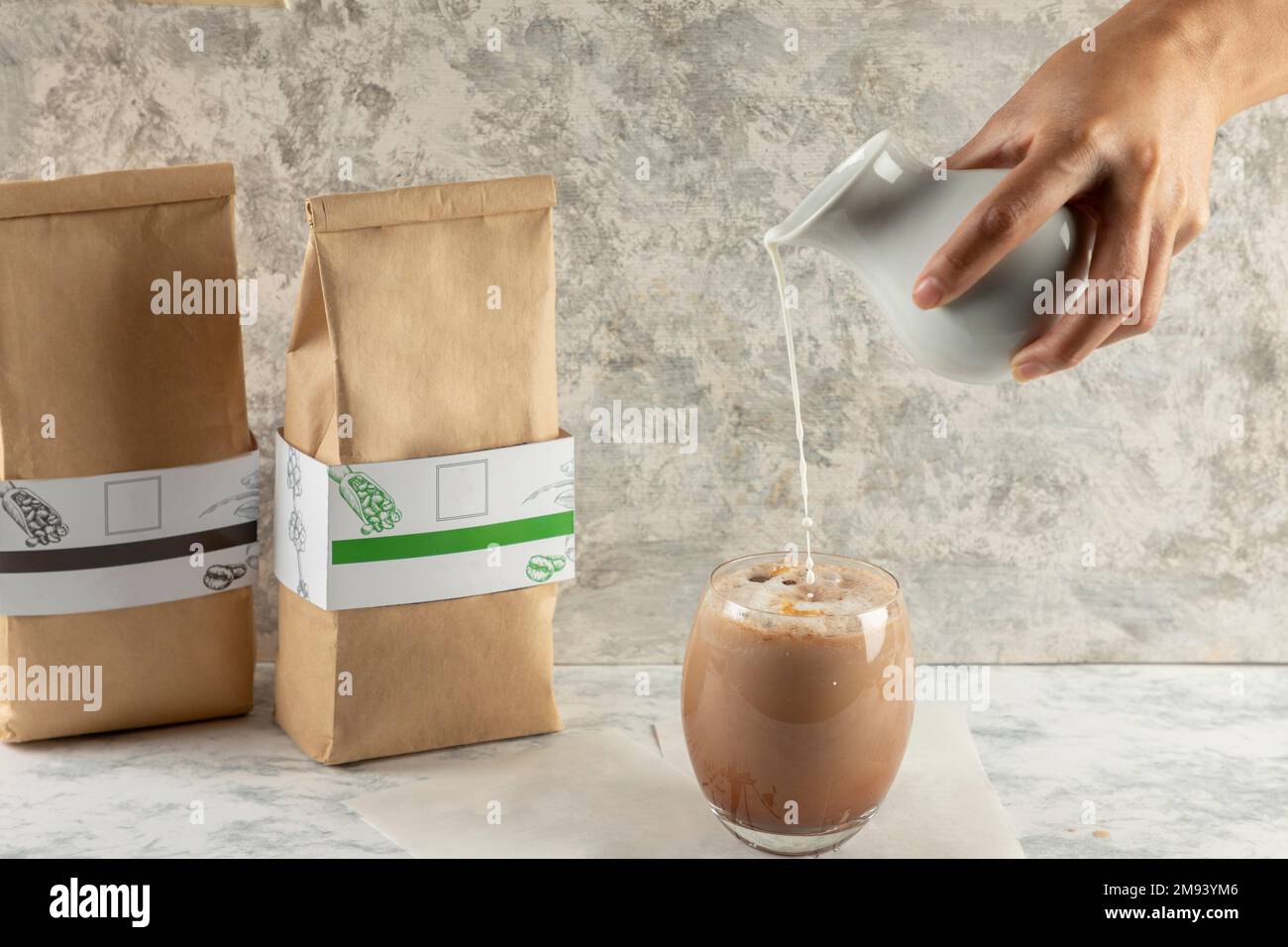 A hand pouring milk over a glass with coffee and two bags of coffee ...