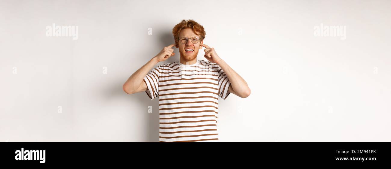 Annoyed redhead guy in glasses shutting ears and complaining loud noise ...