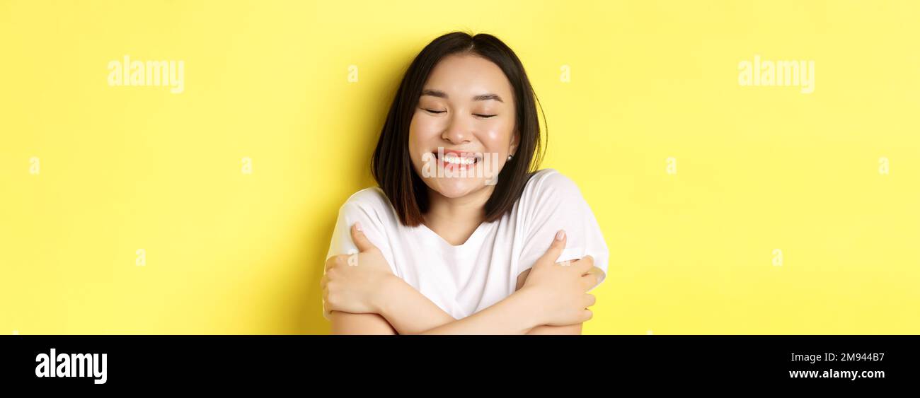 Close up of romantic asian girl hugging herself and dreaming, close ...