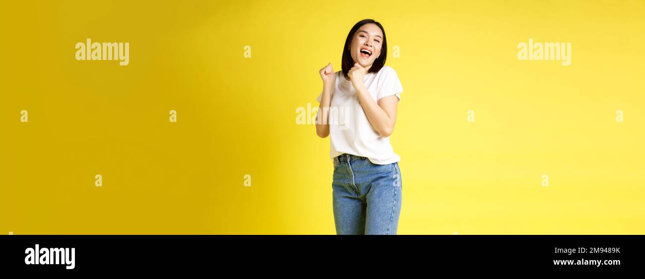 Full size shot of happy asian woman dancing and jumping from happiness ...