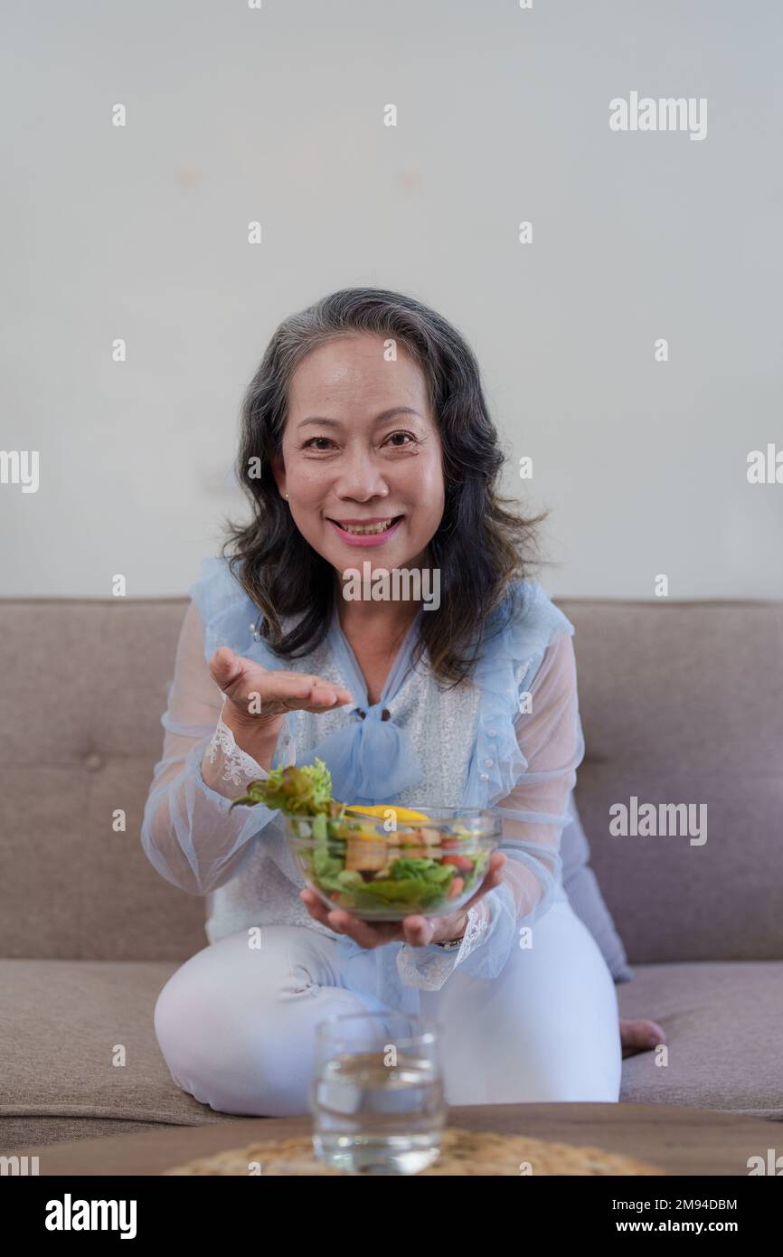 Happy old asian woman eating fresh green salad. Senior woman good healthy at home. Exercise and ...