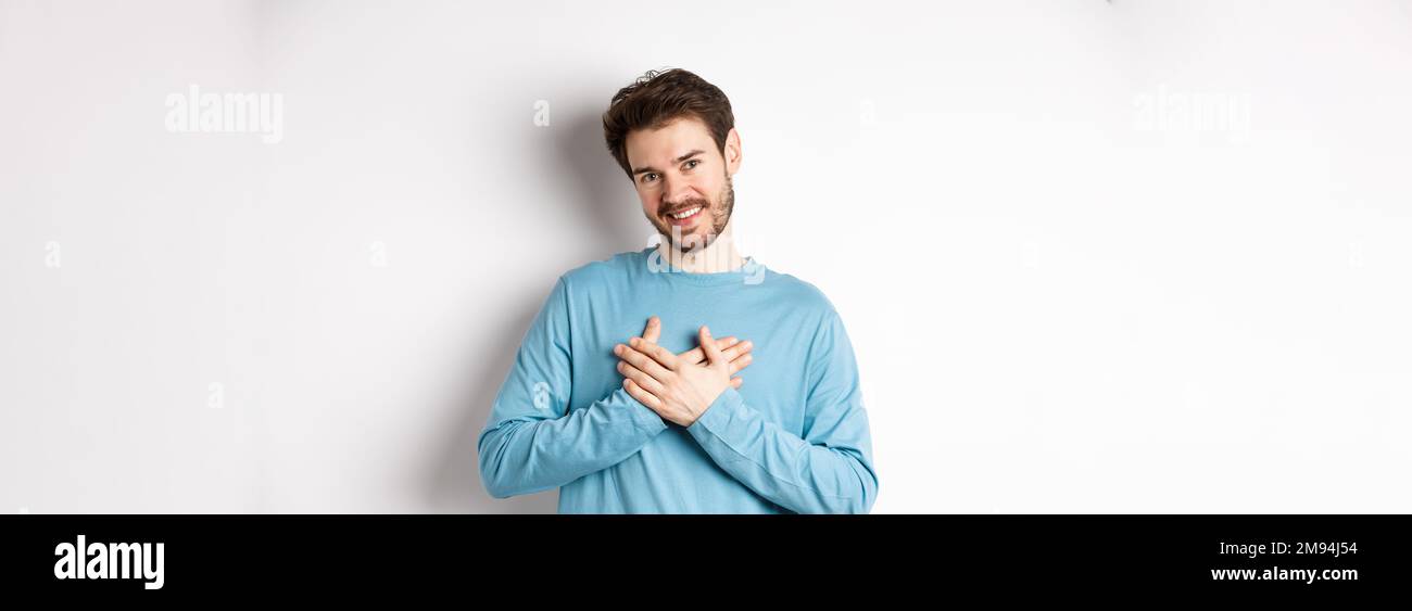 Portrait of young handsome man with beard, holding hands on heart and ...