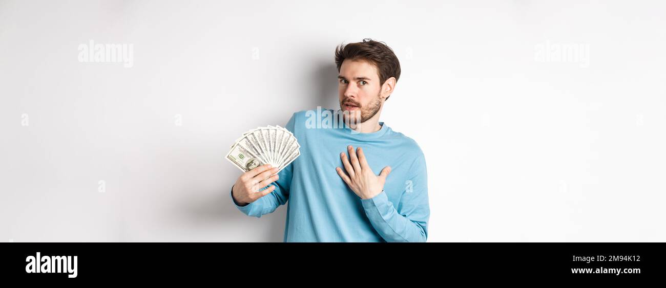 Surprised man holding money, looking amazed at camera, touching chest ...