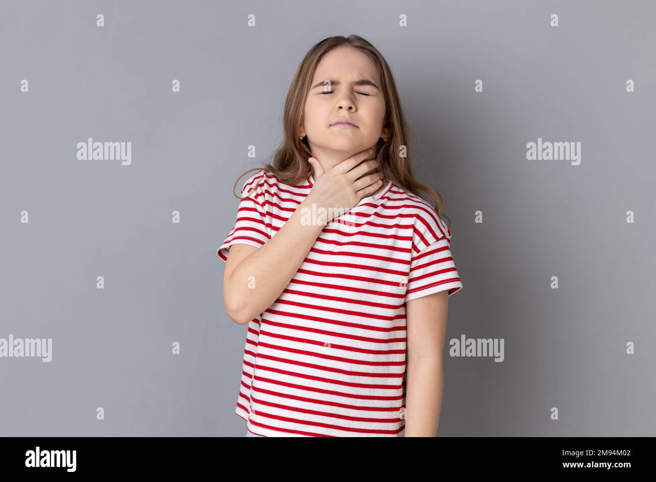 Portrait of little girl wearing striped T-shirt touching neck ...