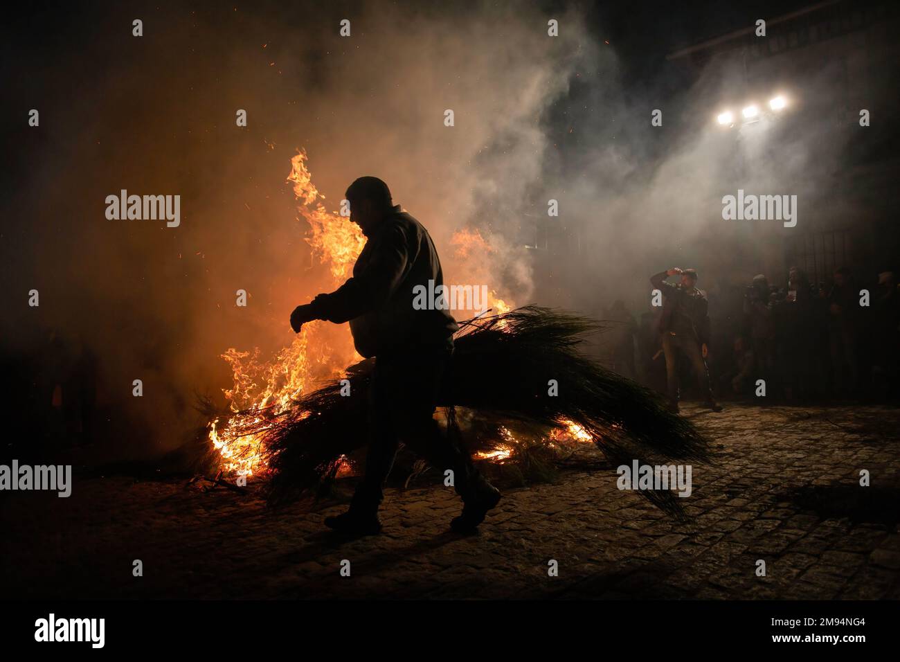 A man carries a bundle of branches to throw on a bonfire during the ...