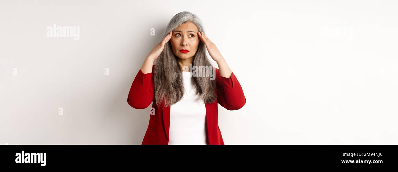 Troubled asian office woman touching head, looking aside and looking ...