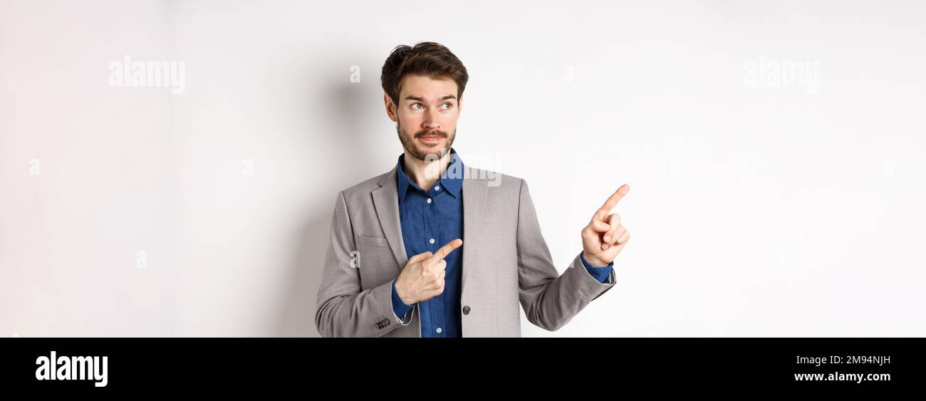 Doubtful male entrepreneur in suit looking and pointing left with ...