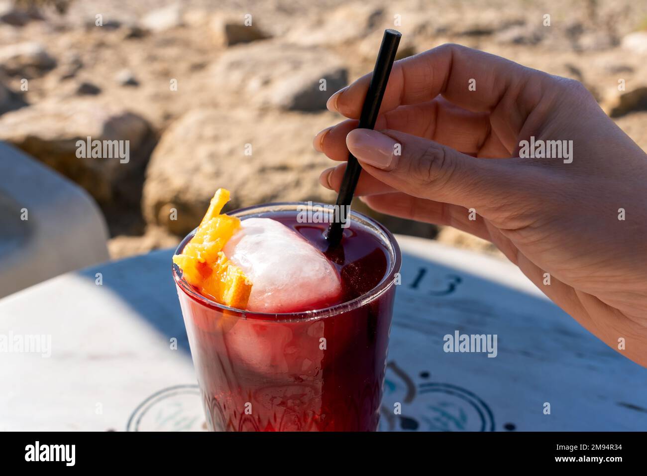 From above of crop anonymous female hand stirring red cocktail in glass ...