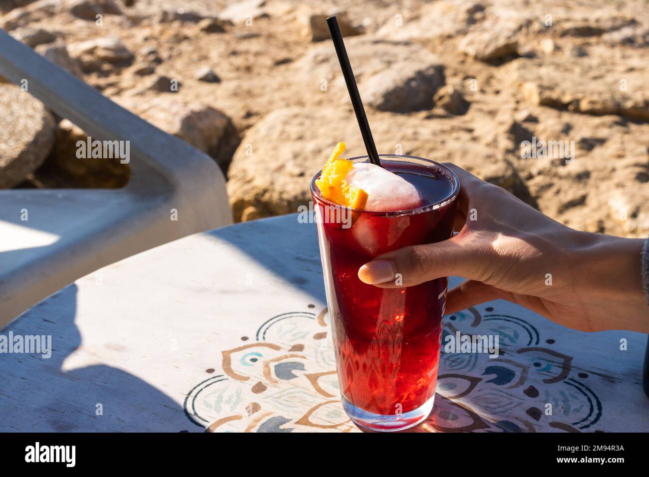 High angle of crop anonymous female hand taking glass of refreshing red cocktail with ice cubes ...