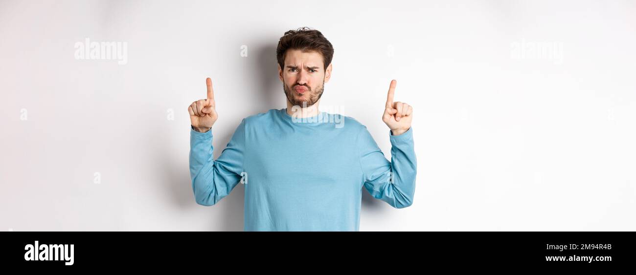 Disappointed male model frowning and sulking, pointing fingers up with ...