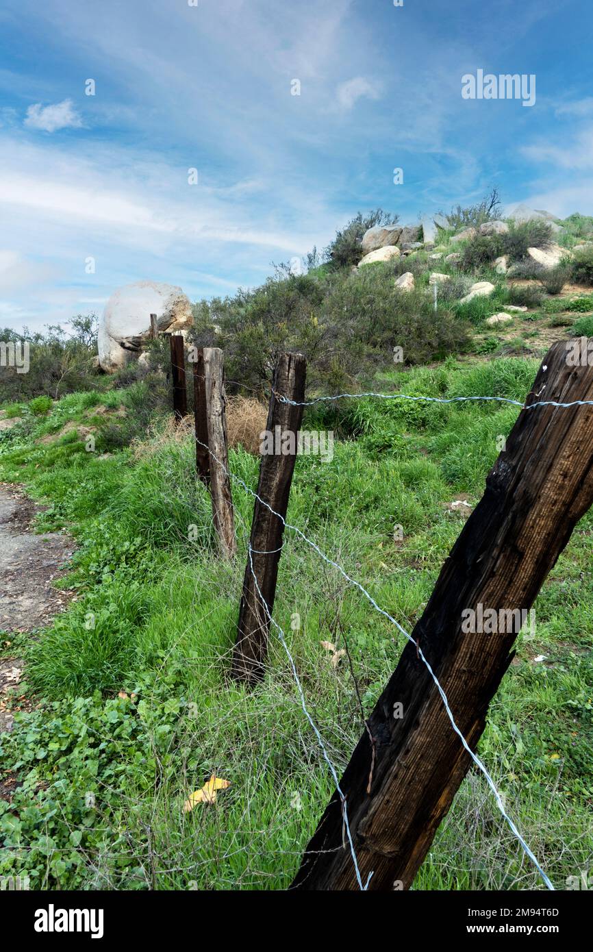Old barbed wire fencing winding toward hill and blue sky in background ...
