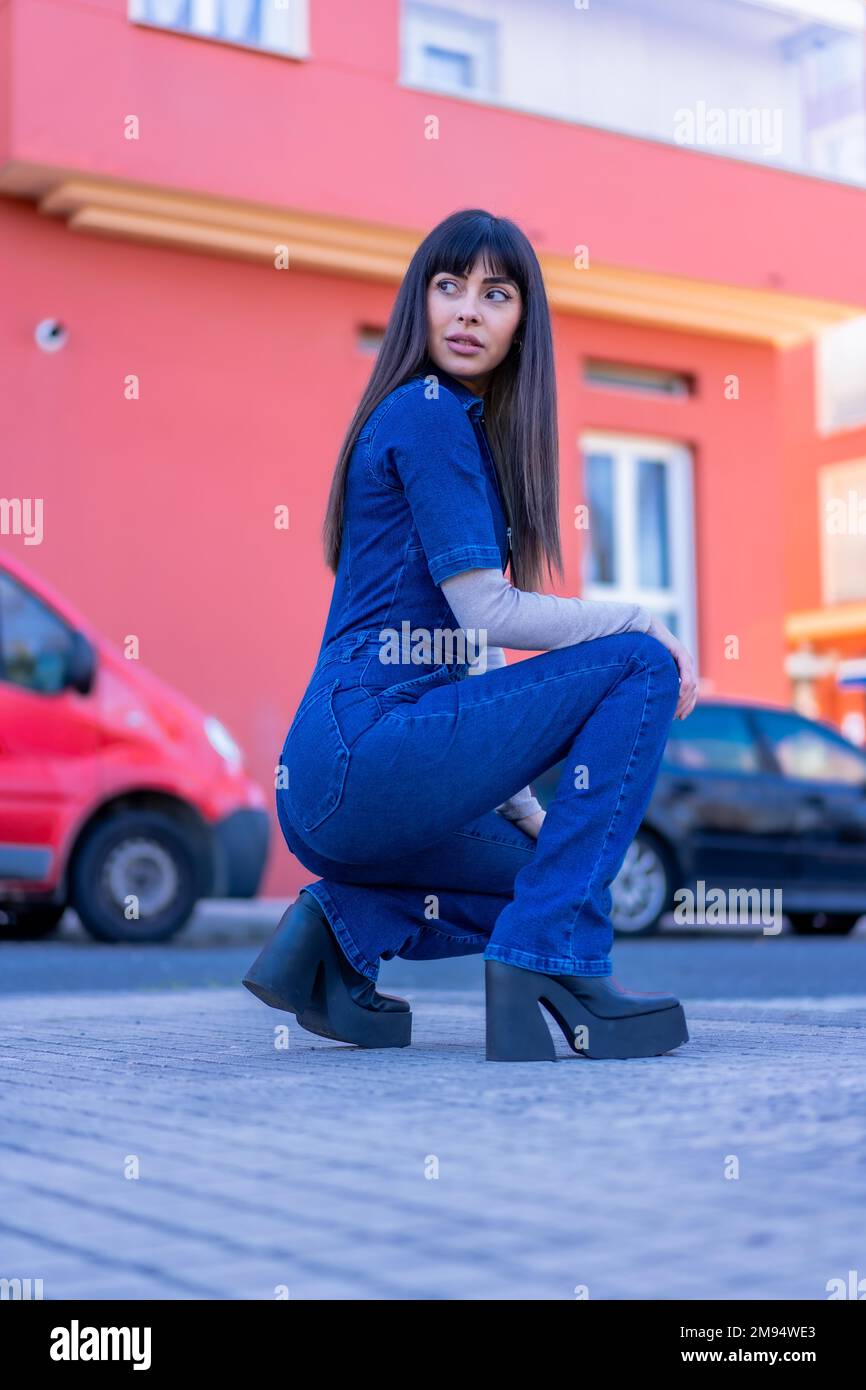 Posing of a brunette model crouching down the street in a denim outfit ...