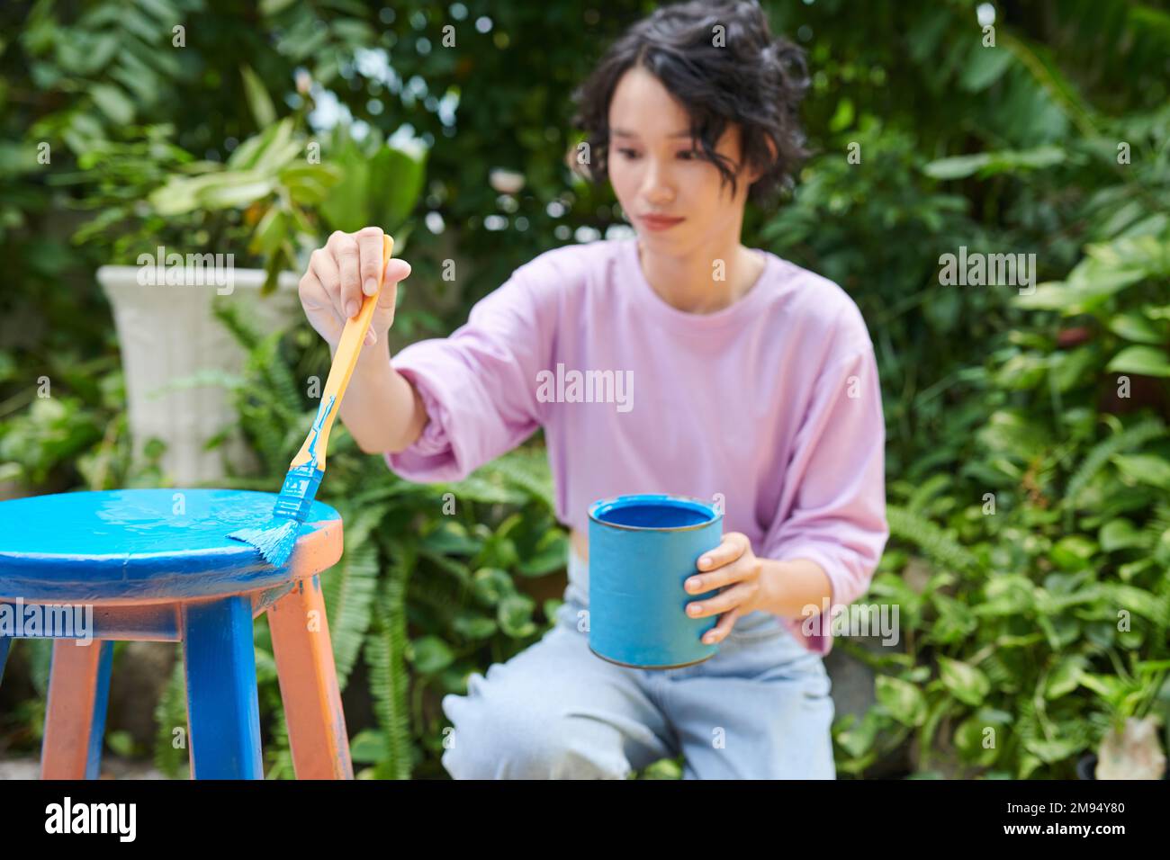 Creative teenage girl painting old wooden chair blue on sunny day Stock ...