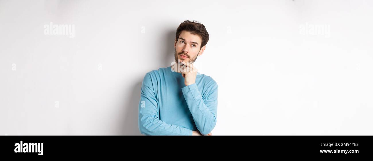 Image of handsome young man making choice, thinking and looking pensive ...