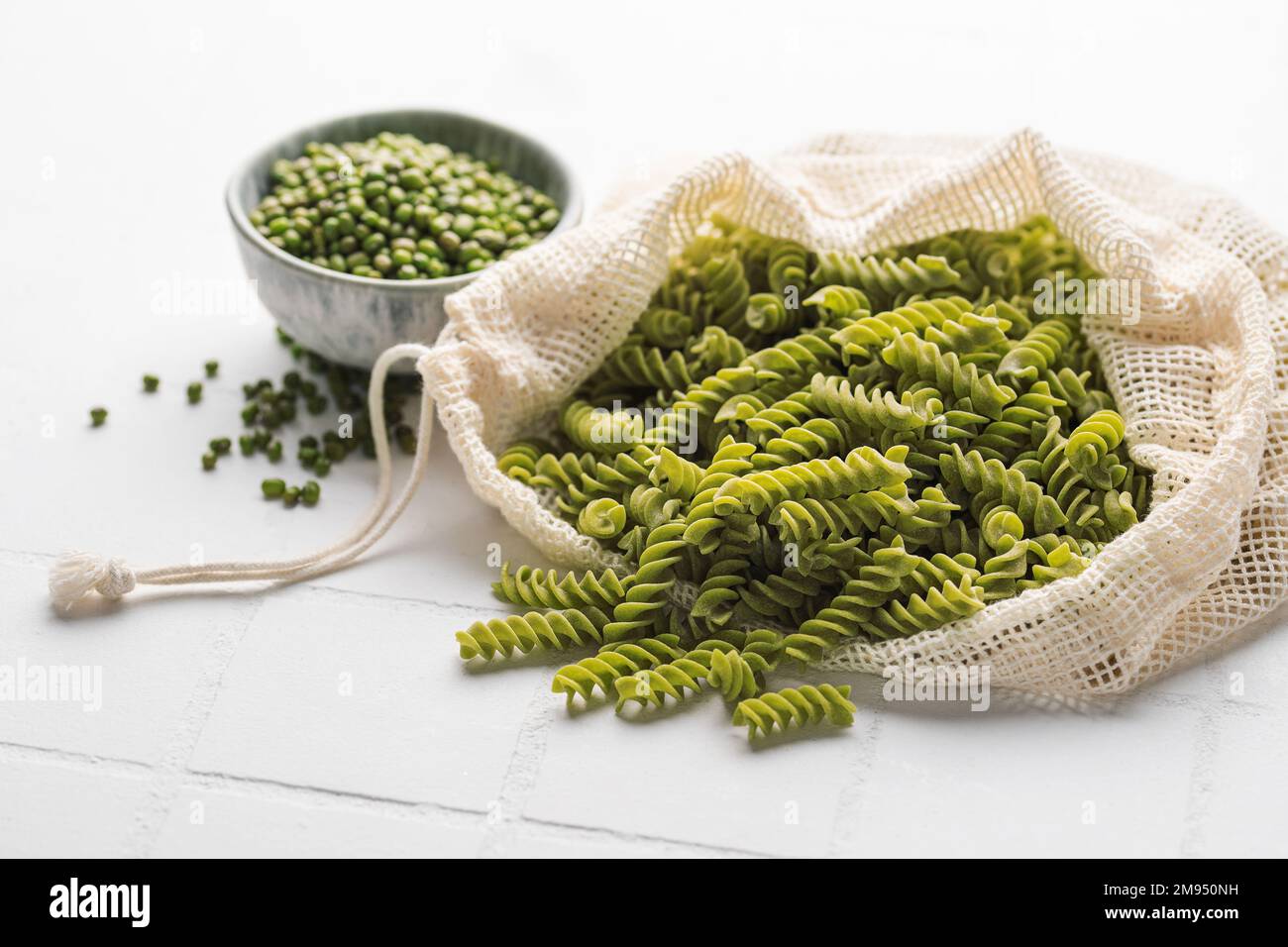 Green mung bean fusilli pasta on a white tile background. Bag with raw ...