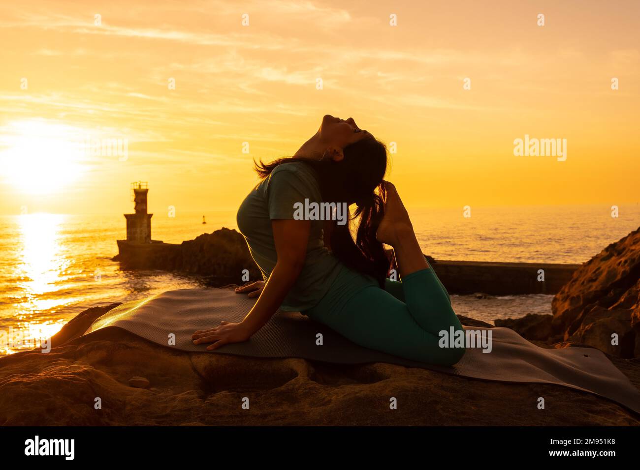 Bhujangasana, A woman doing meditation and yoga exercises at sunset next to a lighthouse in the ...