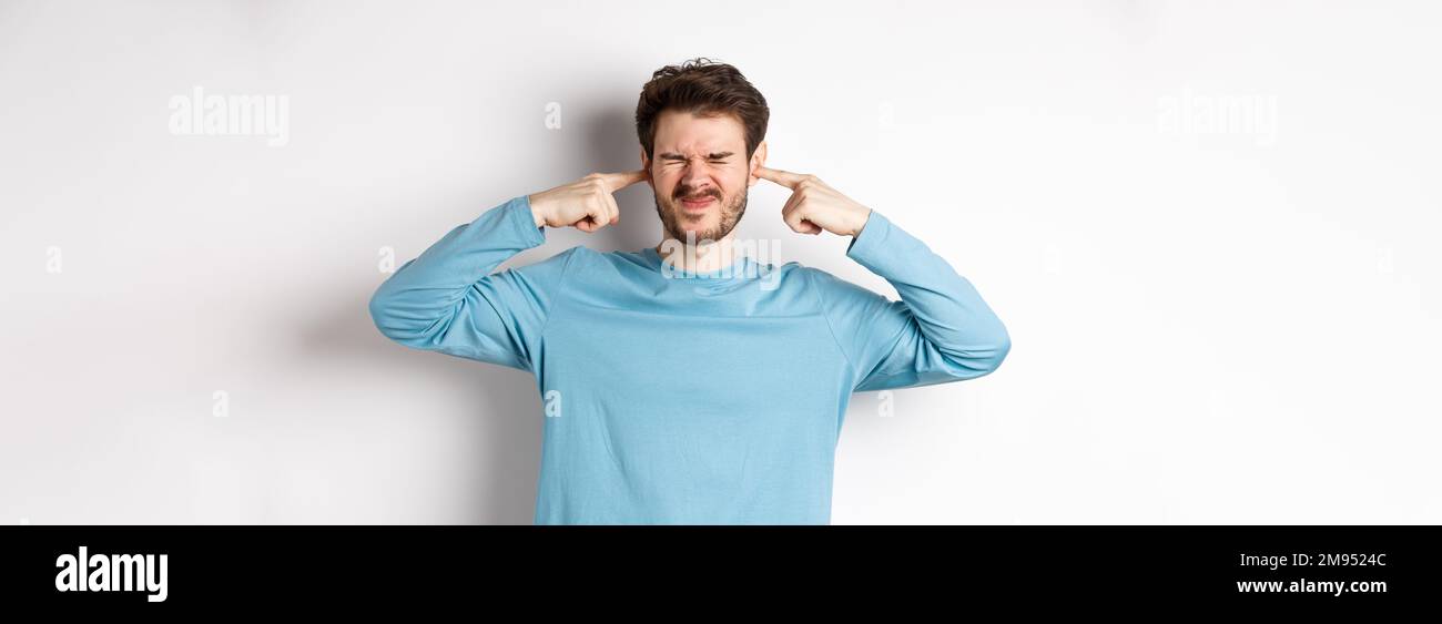 Annoyed young man plug ears from loud awful sound, being disturbed by ...