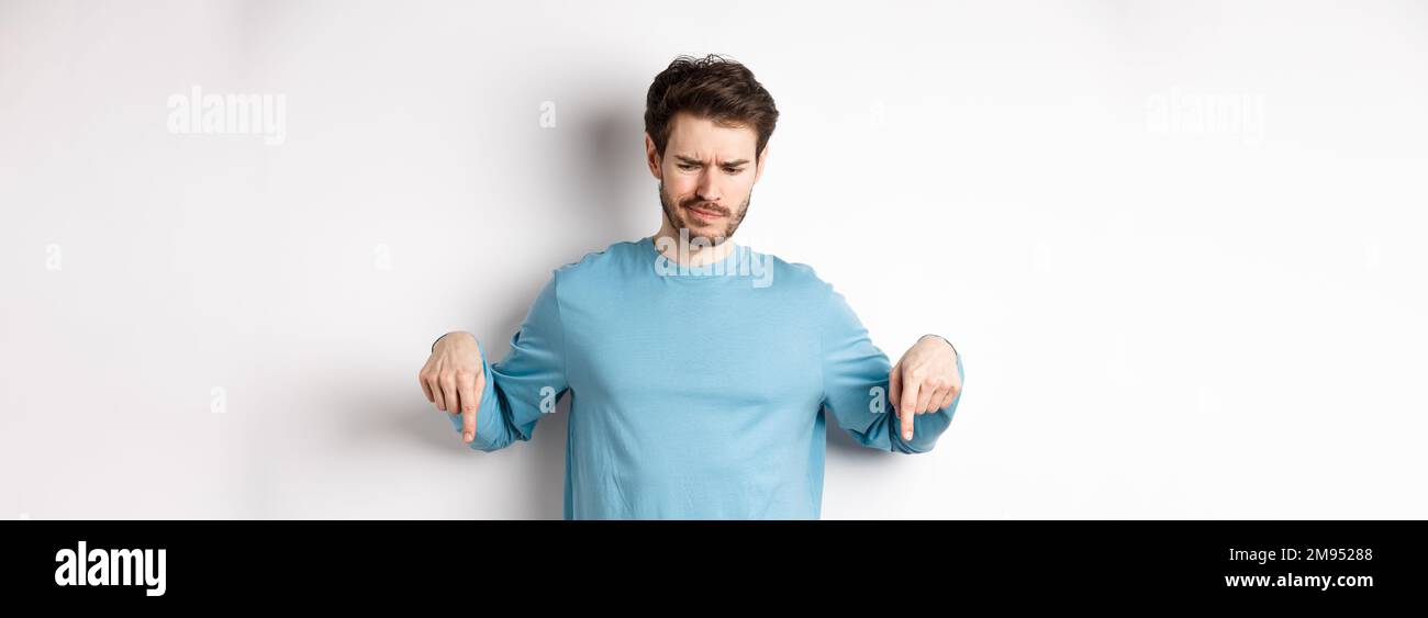 Skeptical boy pointing fingers down and frowning disappointed, looking ...