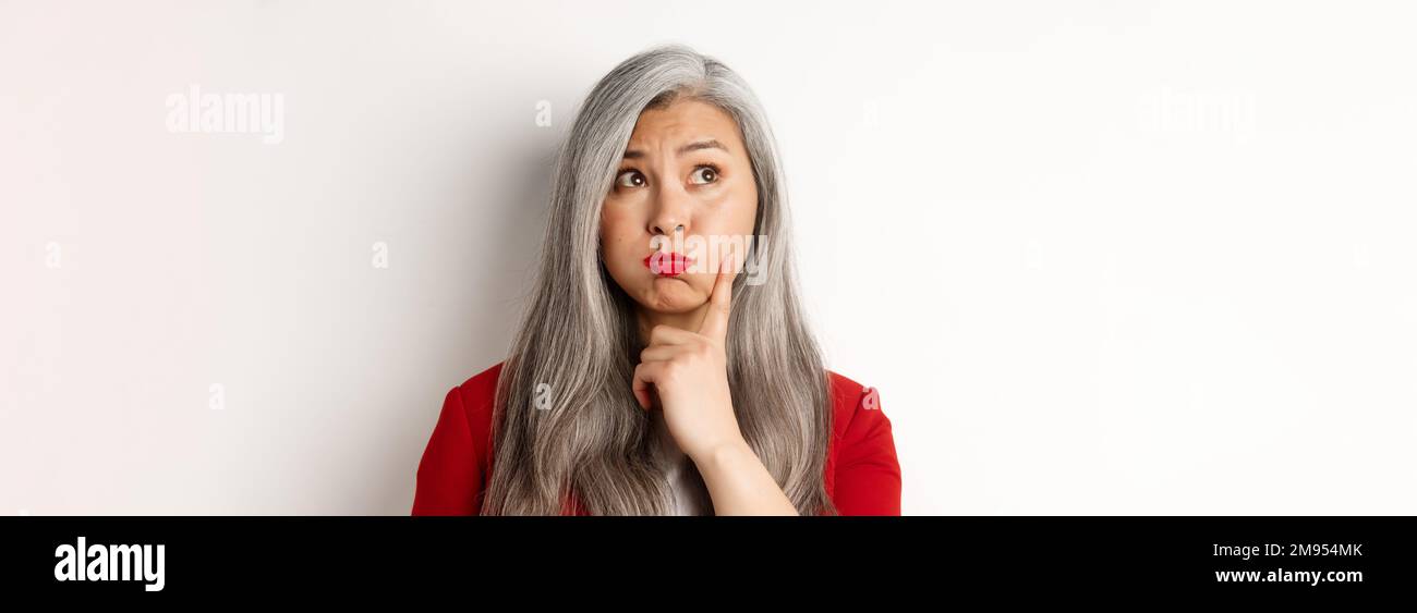 Close up of indecisive asian senior woman making choice, pouting and ...