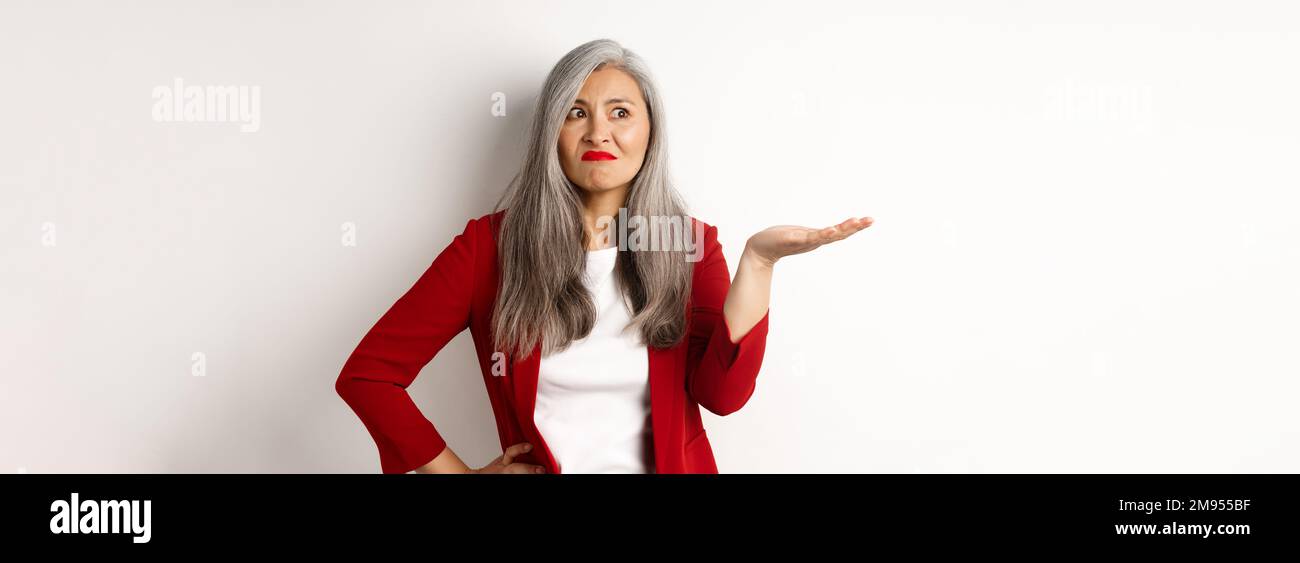 Annoyed and confused asian business woman spread hand sideways and ...