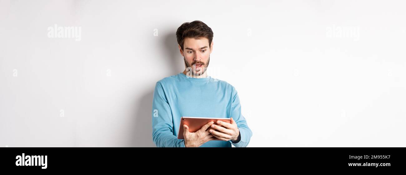 Image of man looking curious at digital tablet, reading interesting ...