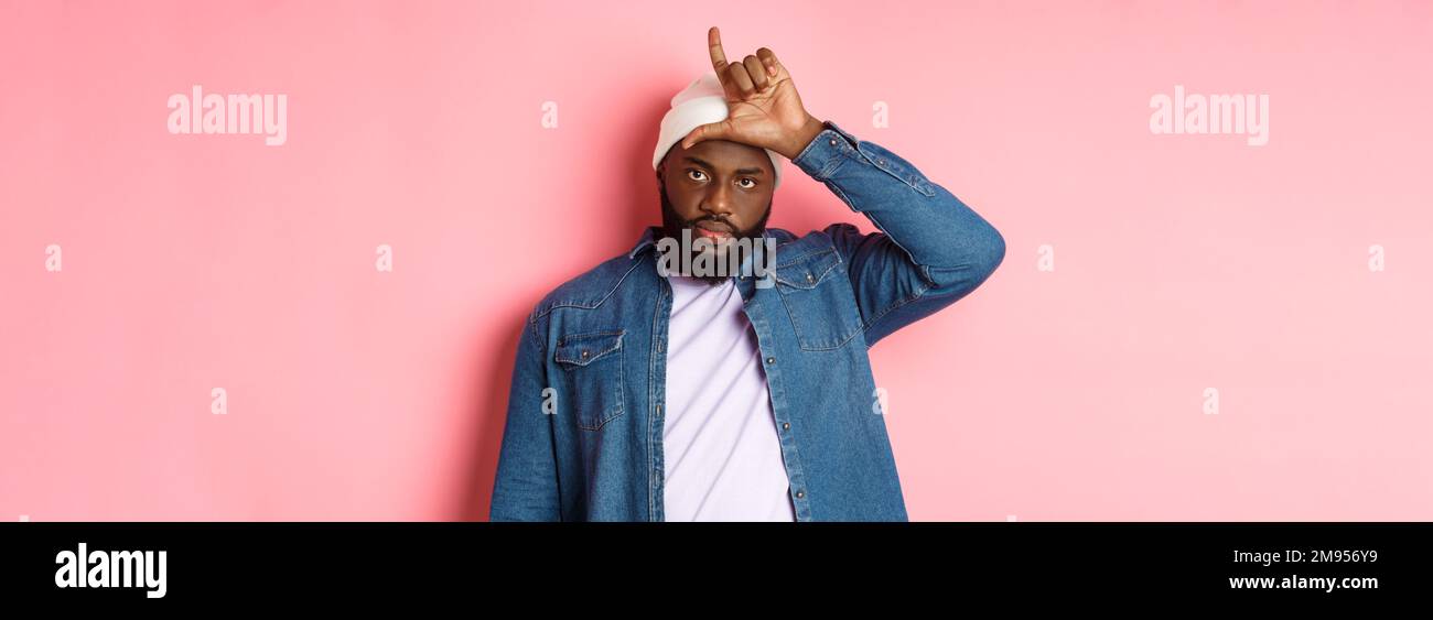 Sad african-american man showing loser sign on forehead and staring at ...