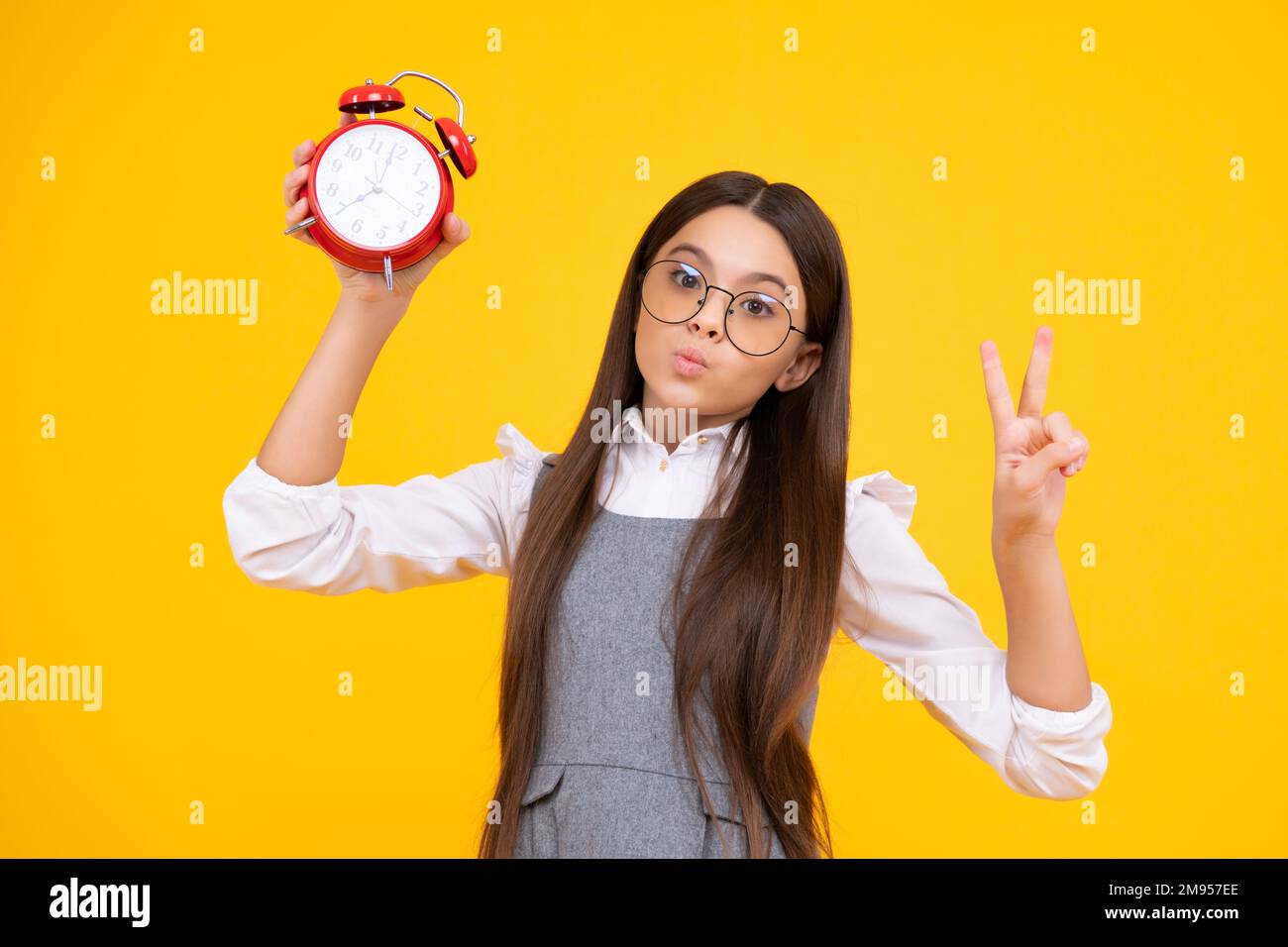 Child teenager girl with alrm clock isolated on yellow background. Time ...