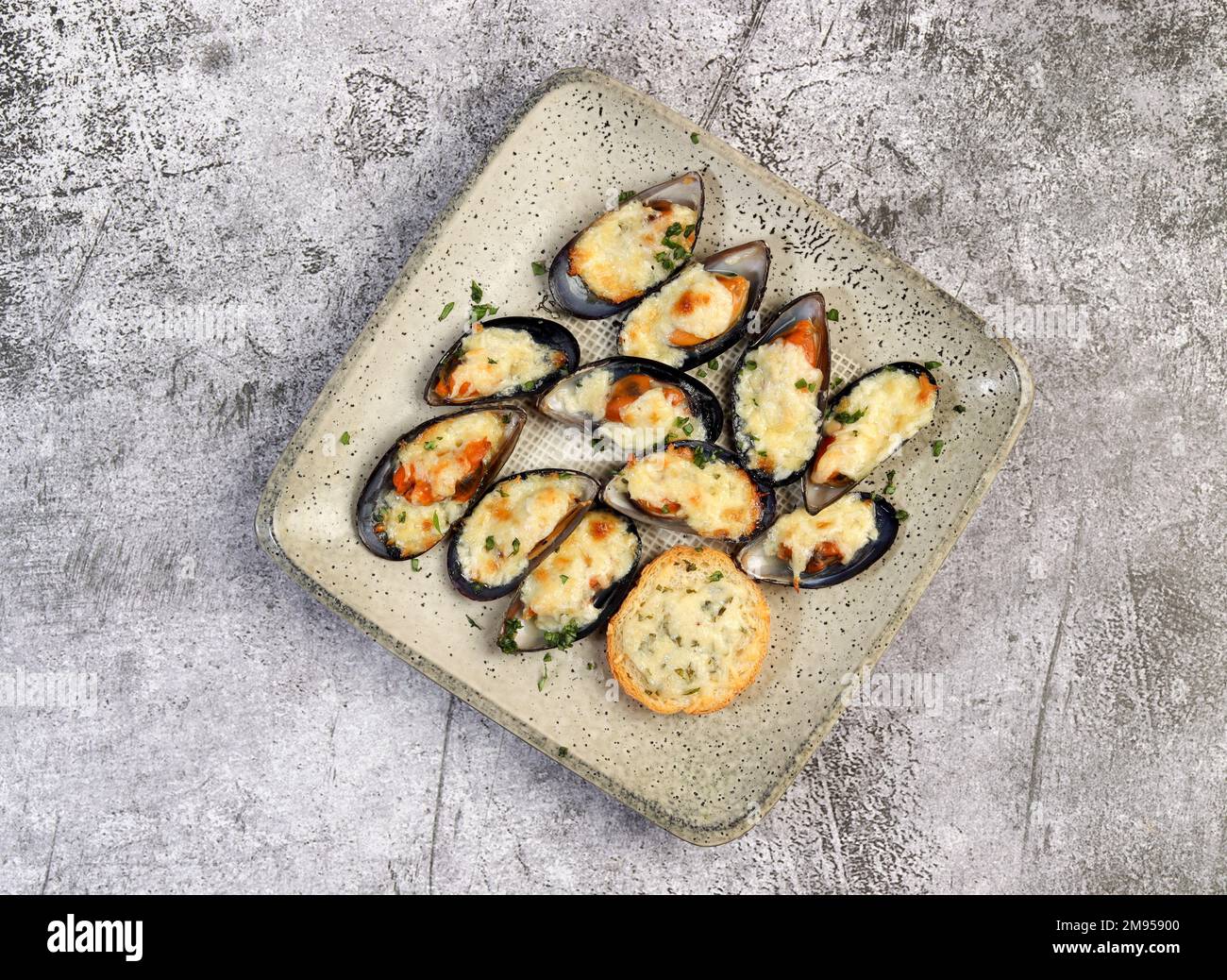 Baked mussels with cheese and herbs on a square plate on a dark ...