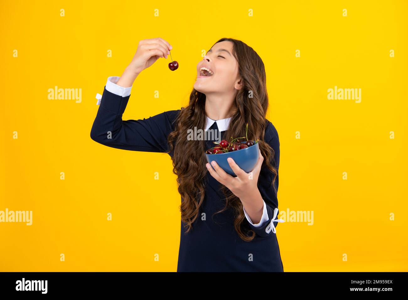 Teenager child girl eating cherries, isolated on yellow background ...