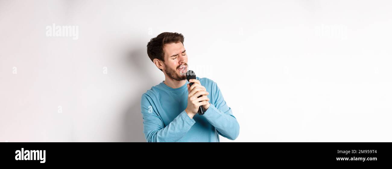 Romantic man singing song in microphone at karaoke, standing over white ...