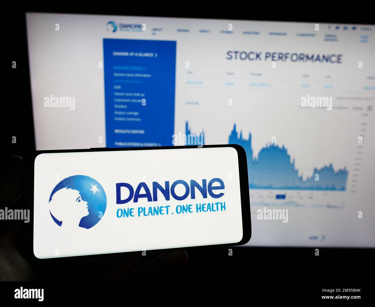 Person holding mobile phone with logo of French food company Danone S.A ...