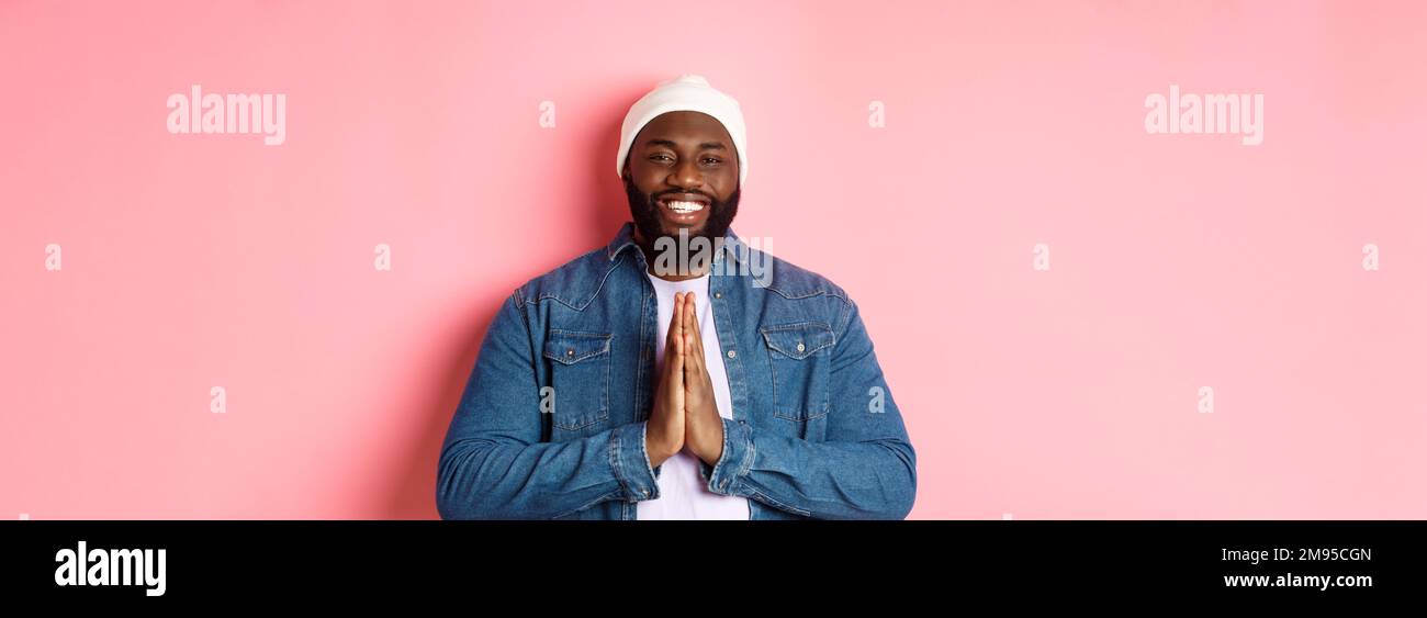 Happy smiling Black man saying thank you, holding hands in pray or ...