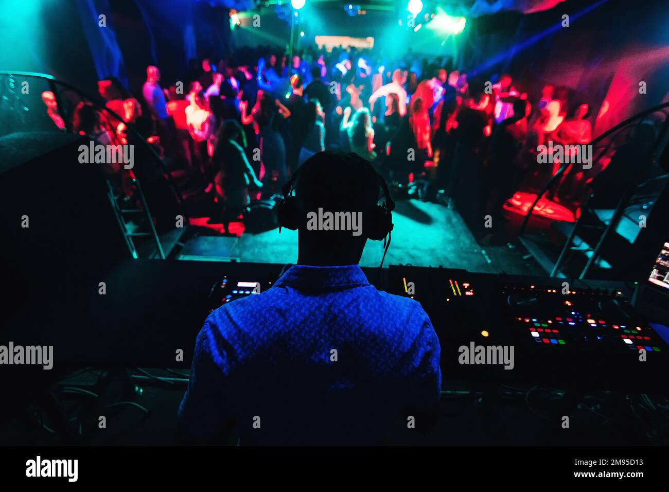 silhouette of a DJ playing music on the mixer and a lot of people ...