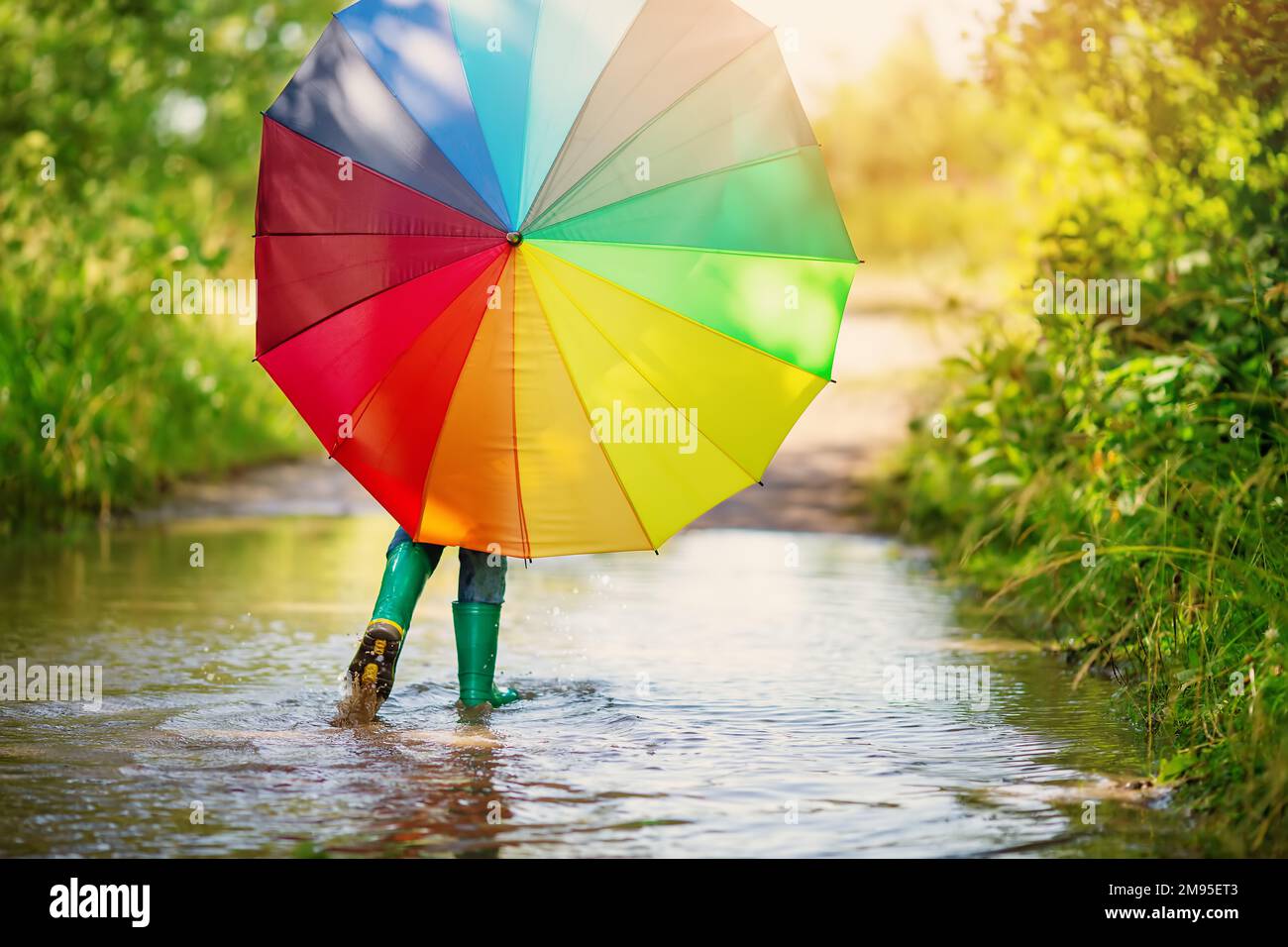 Boy walking through the puddle with colorful umbrella in his hands ...