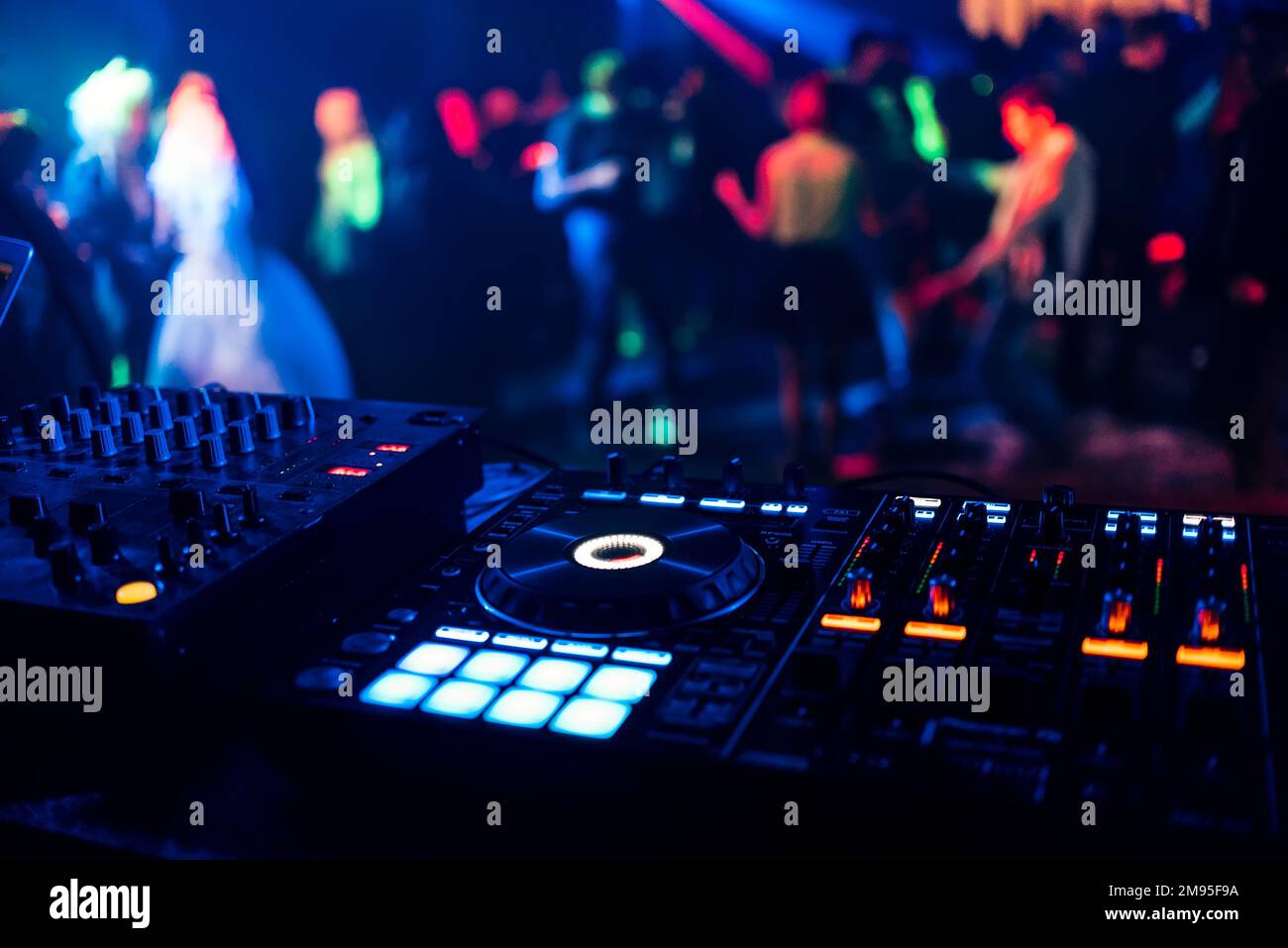 control DJ for mixing music with blurred people dancing at a party in a ...