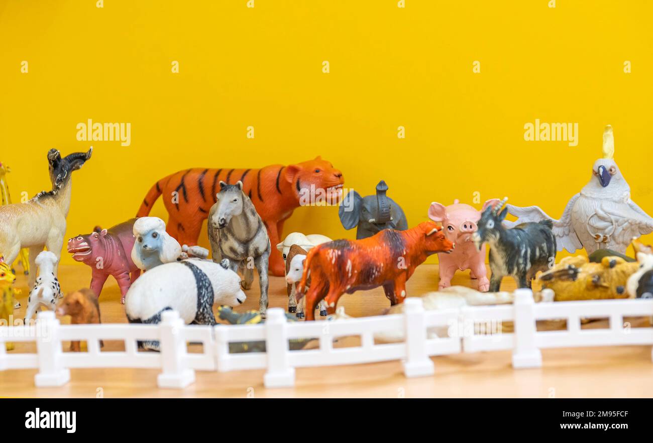 Different toy animal models stand on wooden table behind a white fence ...
