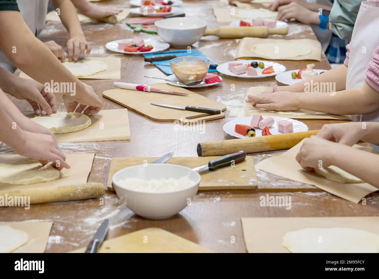 Long kitchen table with food ingredients and utensils, around which ...