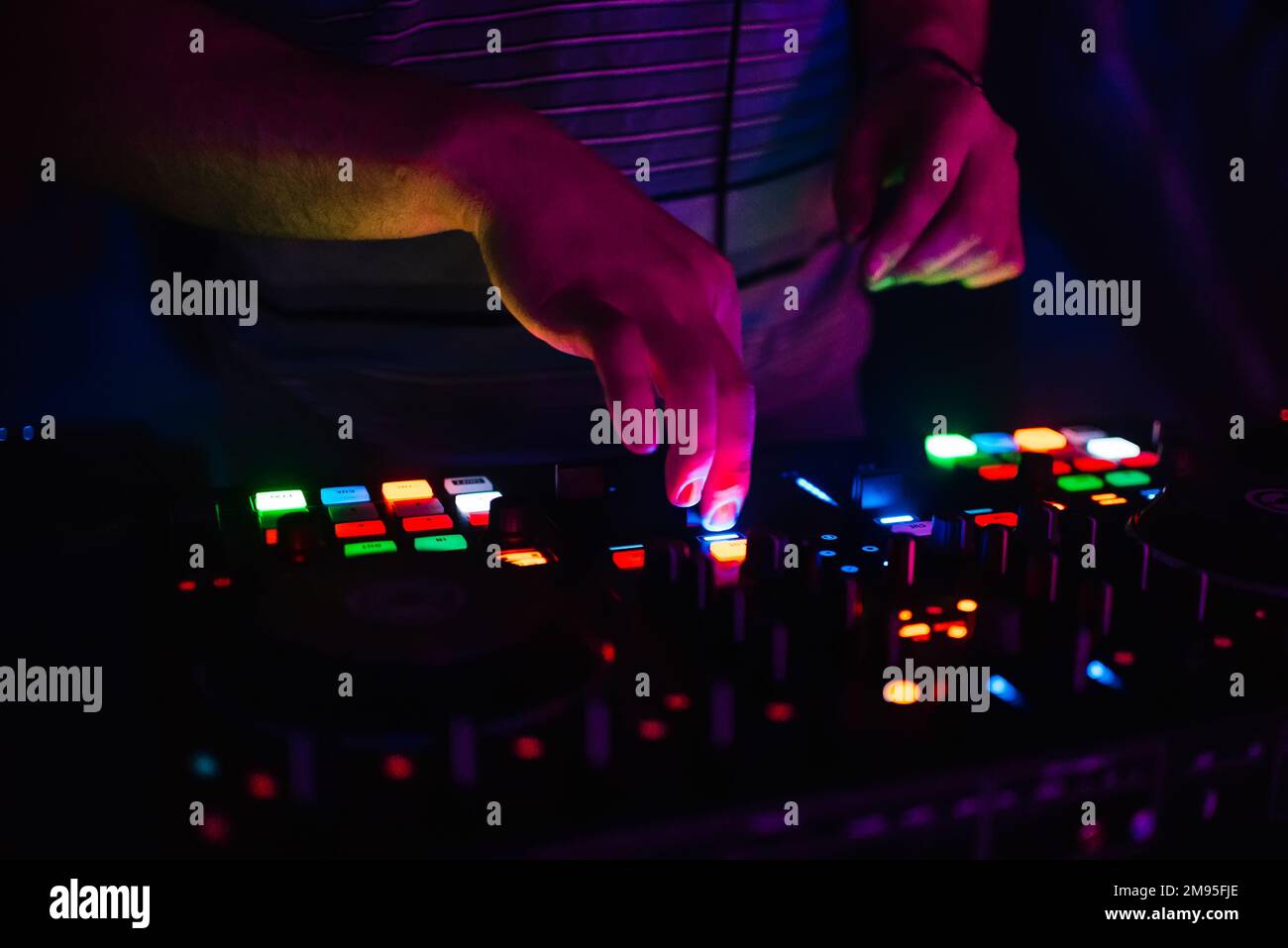 hands on professional DJ mixer with multi-colored glowing buttons ...
