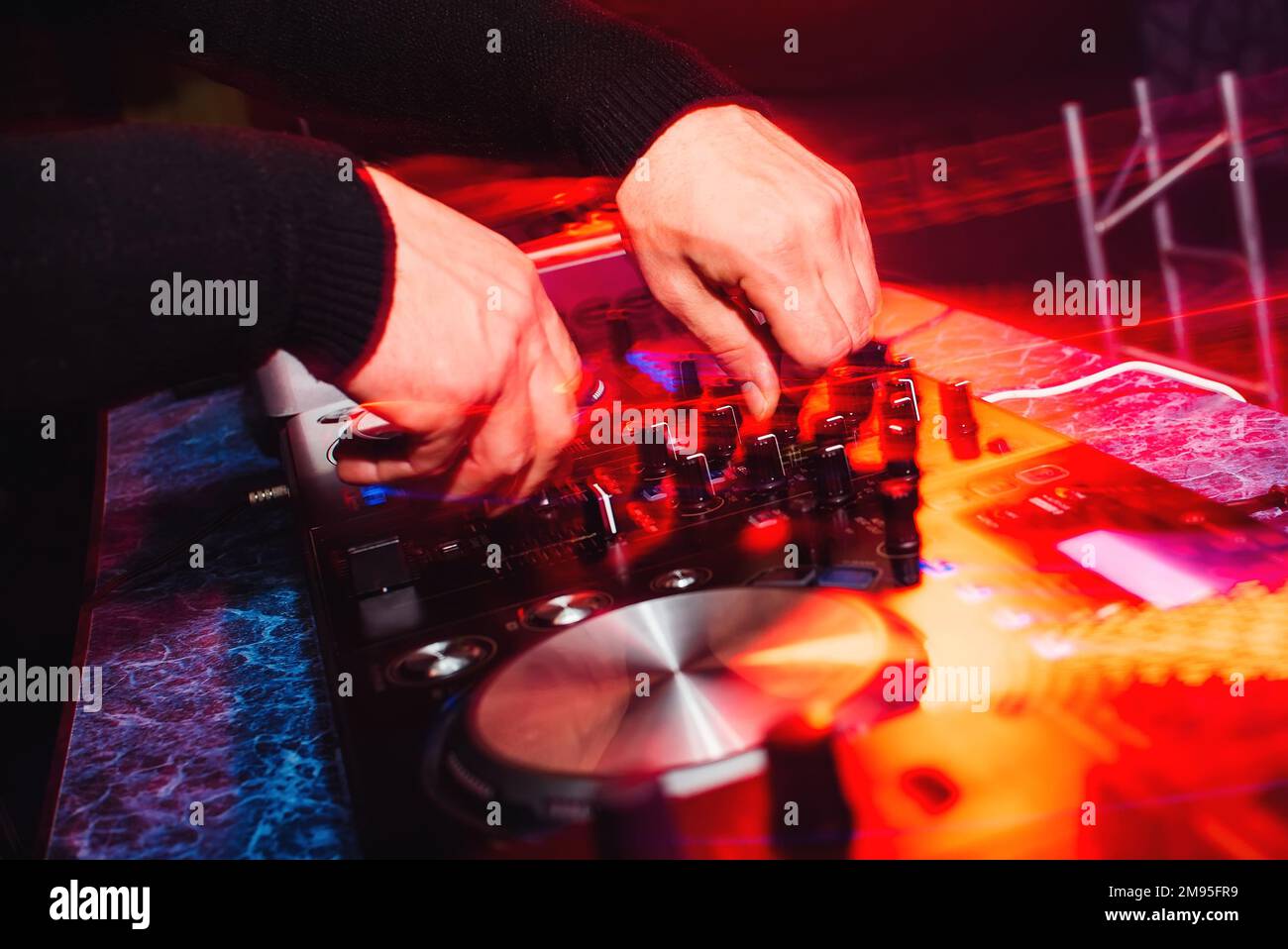 hands of a professional DJ playing and mixing music with bright light ...