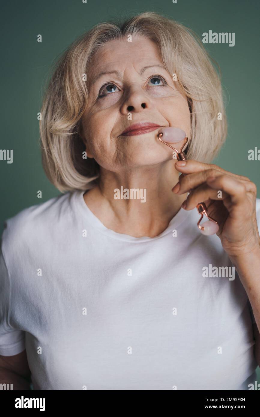 Mature woman doing lifting treatment for wrinkles using jade roller ...